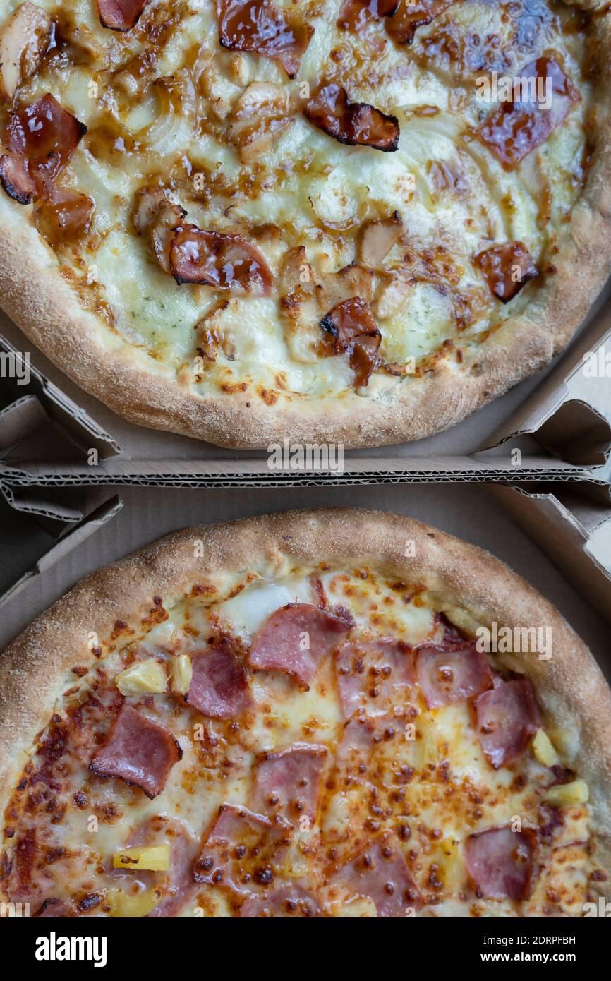 Closeup vertical view of two pizzas on cardboard boxes.Hawaiian and ...