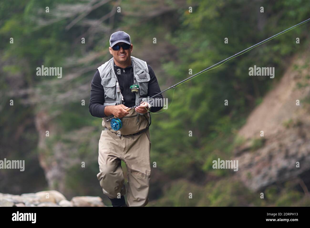 Smiling fisherman in glasses, cap and uniform holding rod while ...