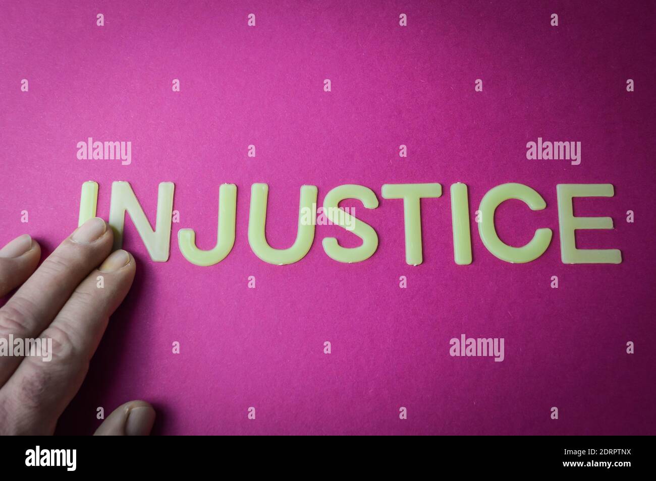 Human fingers holding the word Injustice, written with plastic letters ...