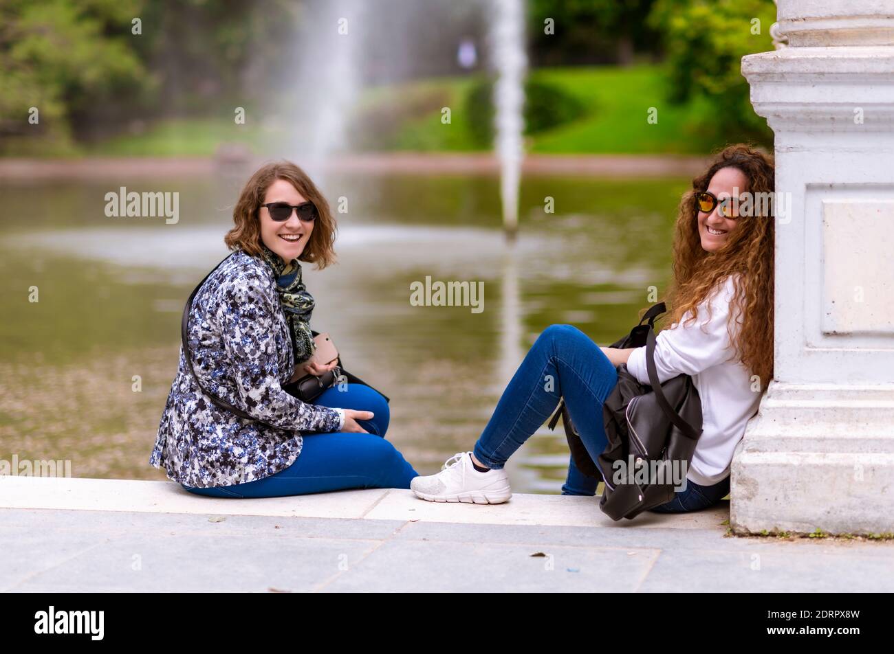 Talking sitting on a lake with fountain, they are mother and daughter ...