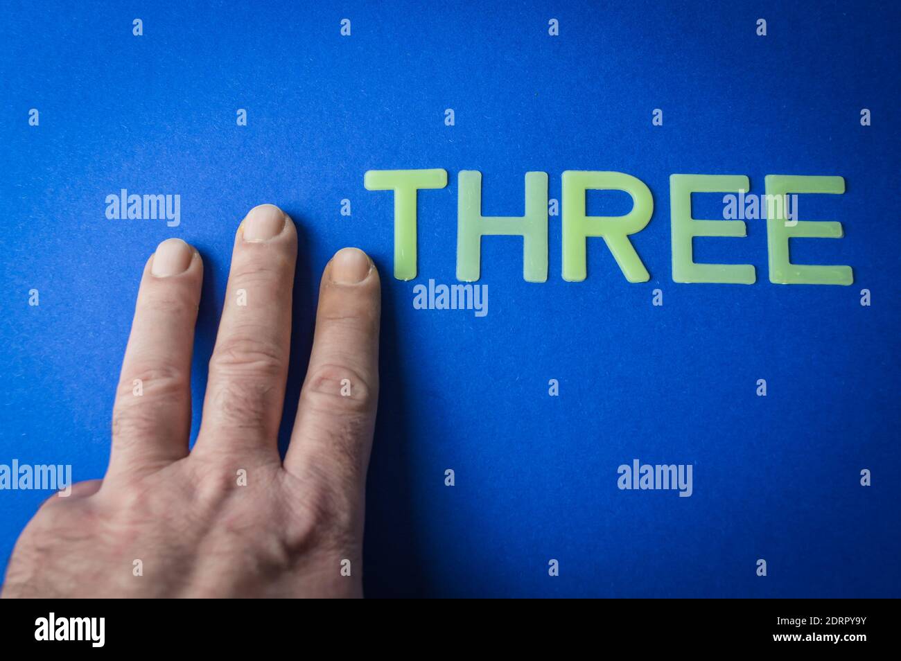 Three human fingers beside the word Three written with plastic letters ...