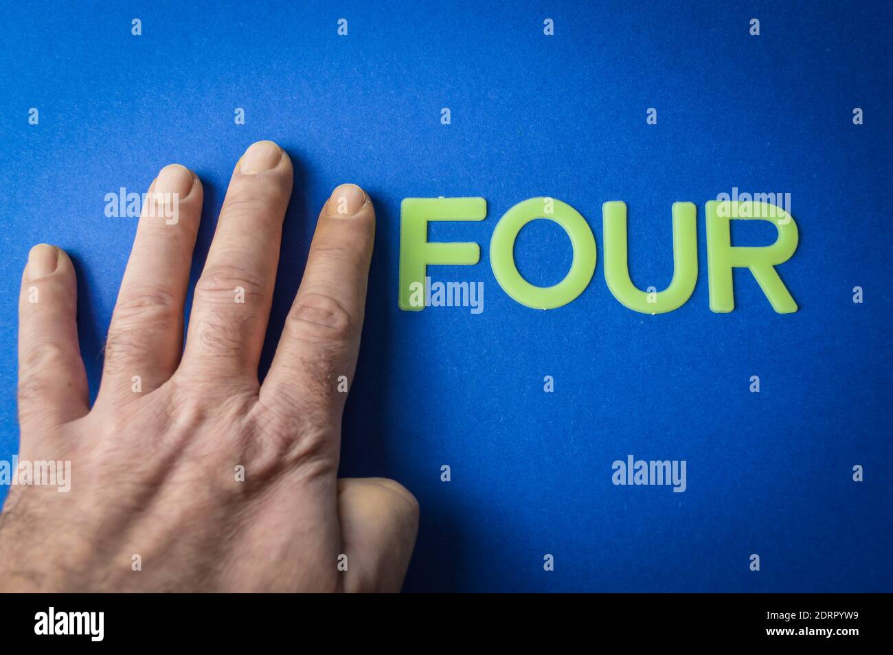 Four human fingers beside the word Four written with plastic letters on ...