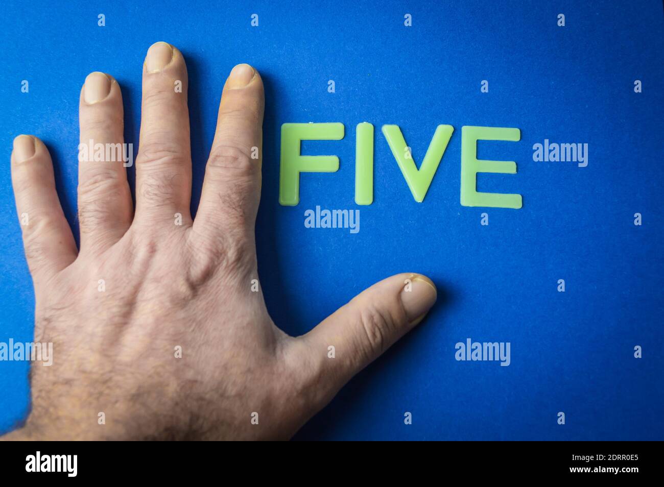 Five human fingers beside the word Five written with plastic letters on ...