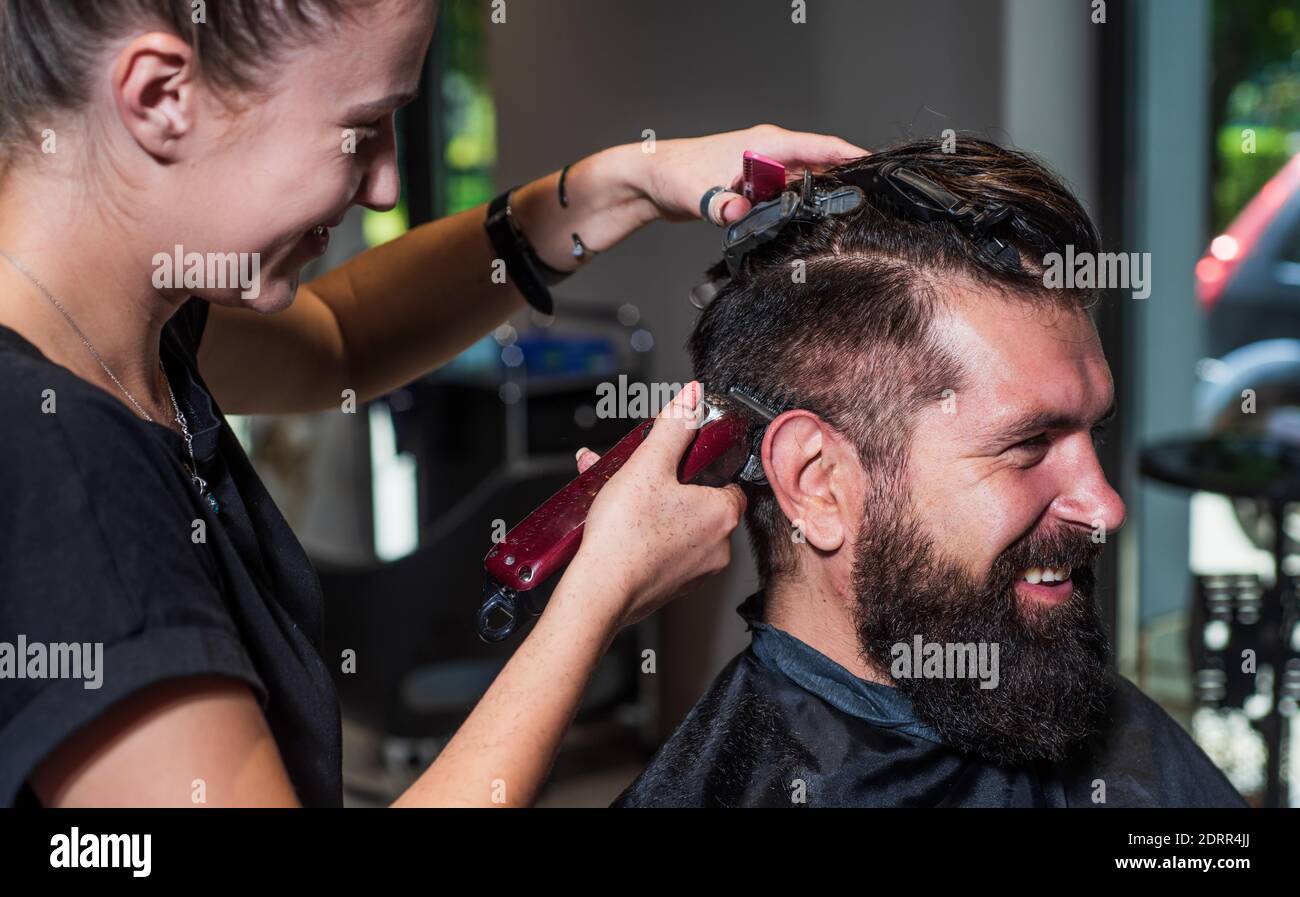 attractive barber making haircut of handsome guy in barbershop ...