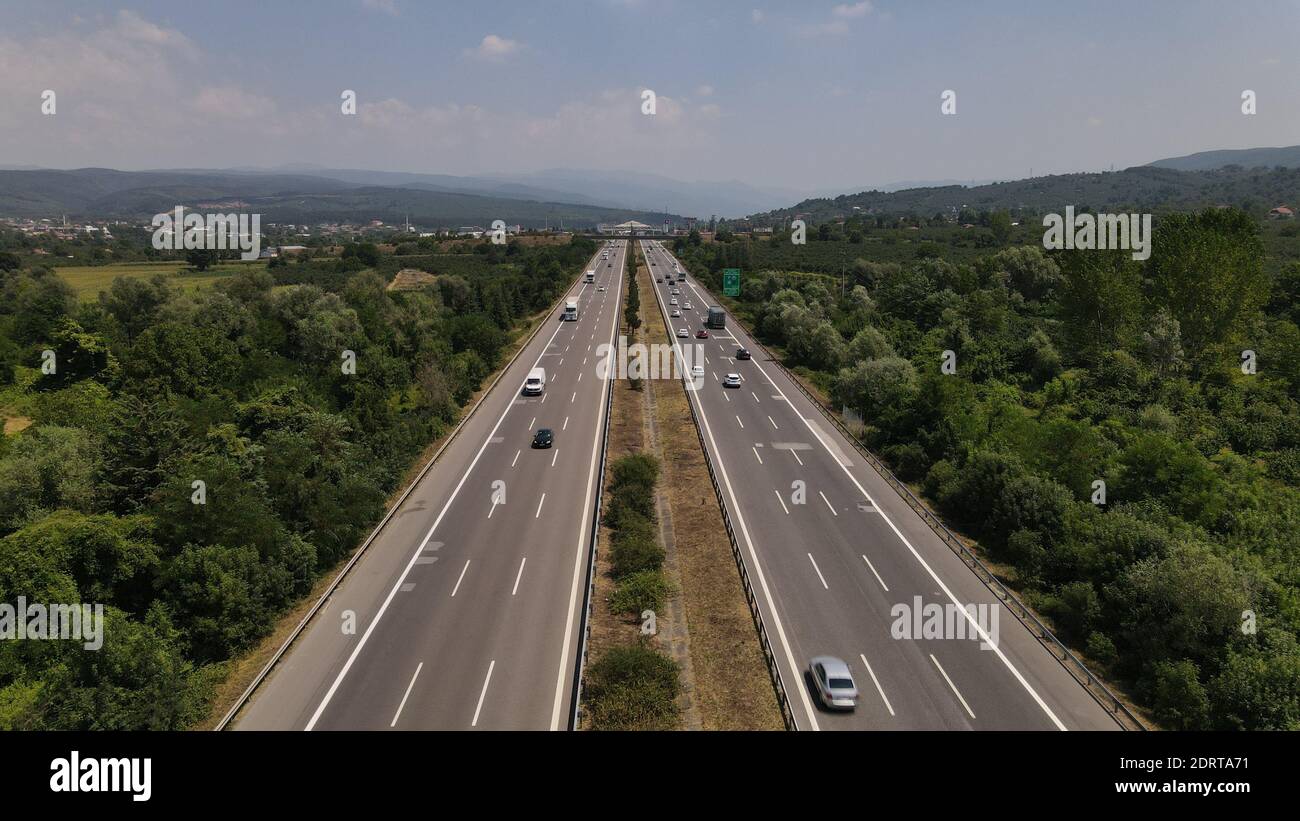 A drone view of a two-lane road surrounded by trees under the sunlight ...