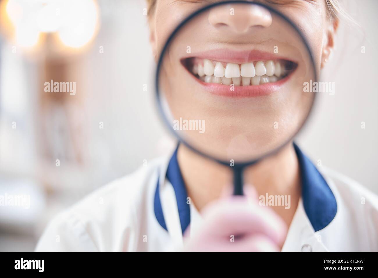 Joyful female dentist smiling through magnifier in office Stock Photo ...