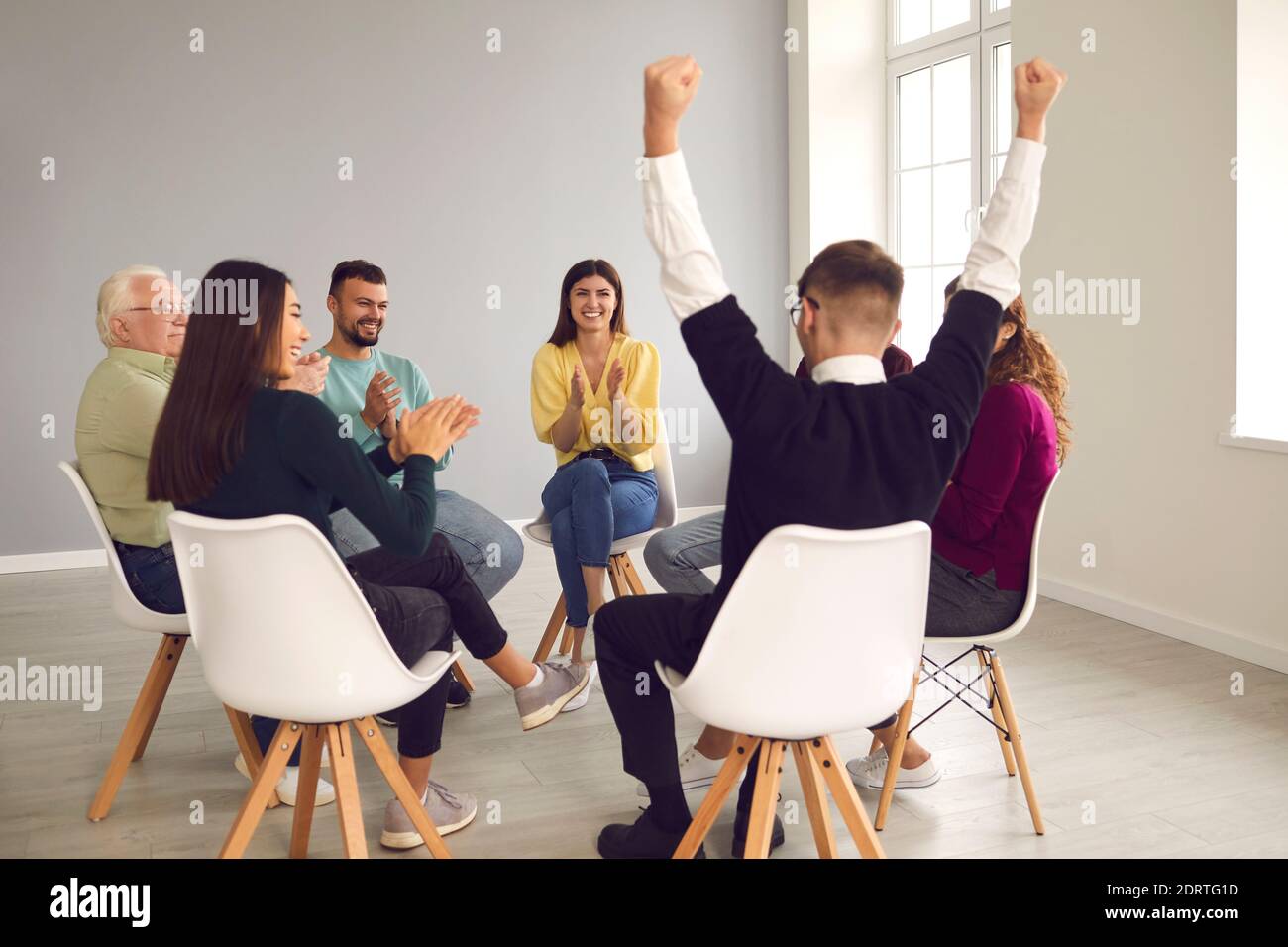Diverse group therapy members applauding happy young man who overcame ...