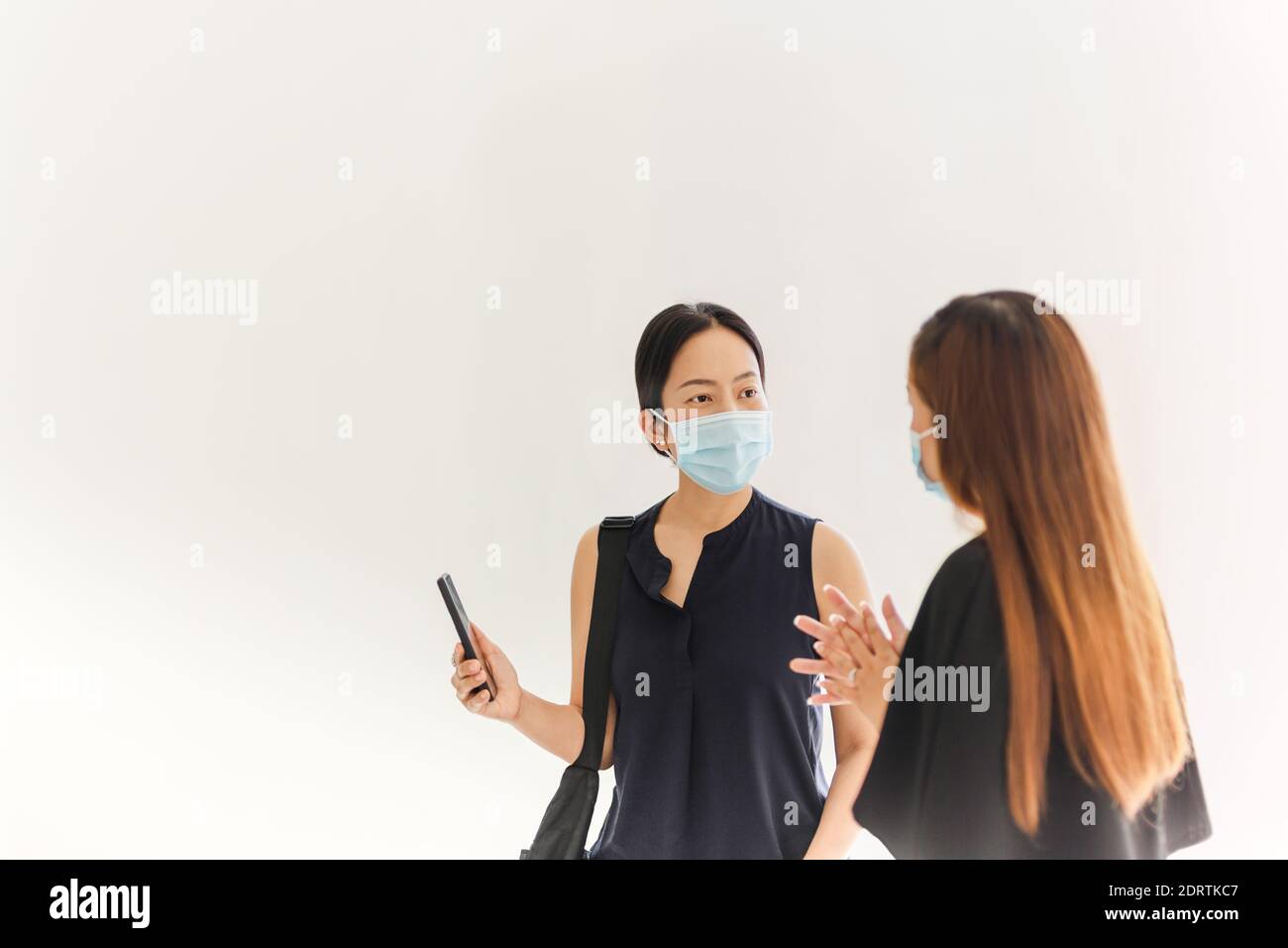 Two female in social distance wearing face mask talking in white ...