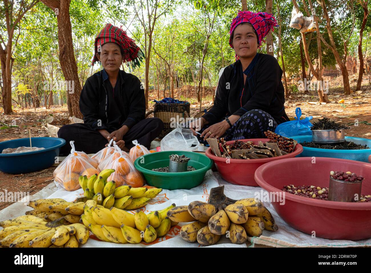 Two Burmese women sitting next to a fruit and nut stall on the ground ...