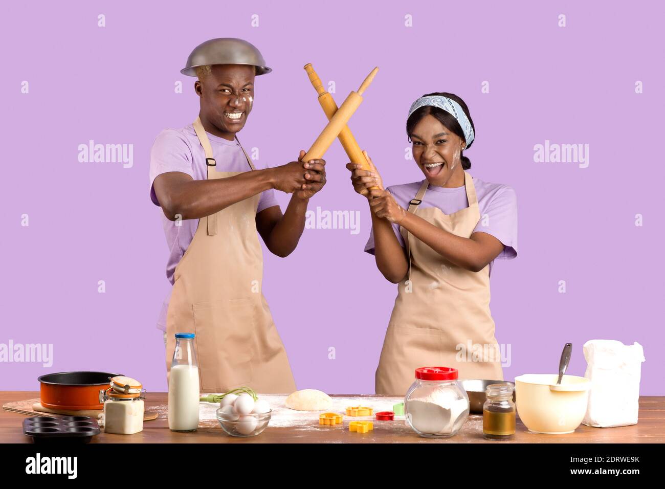 Silly African American couple having mock fight with rolling pins while ...