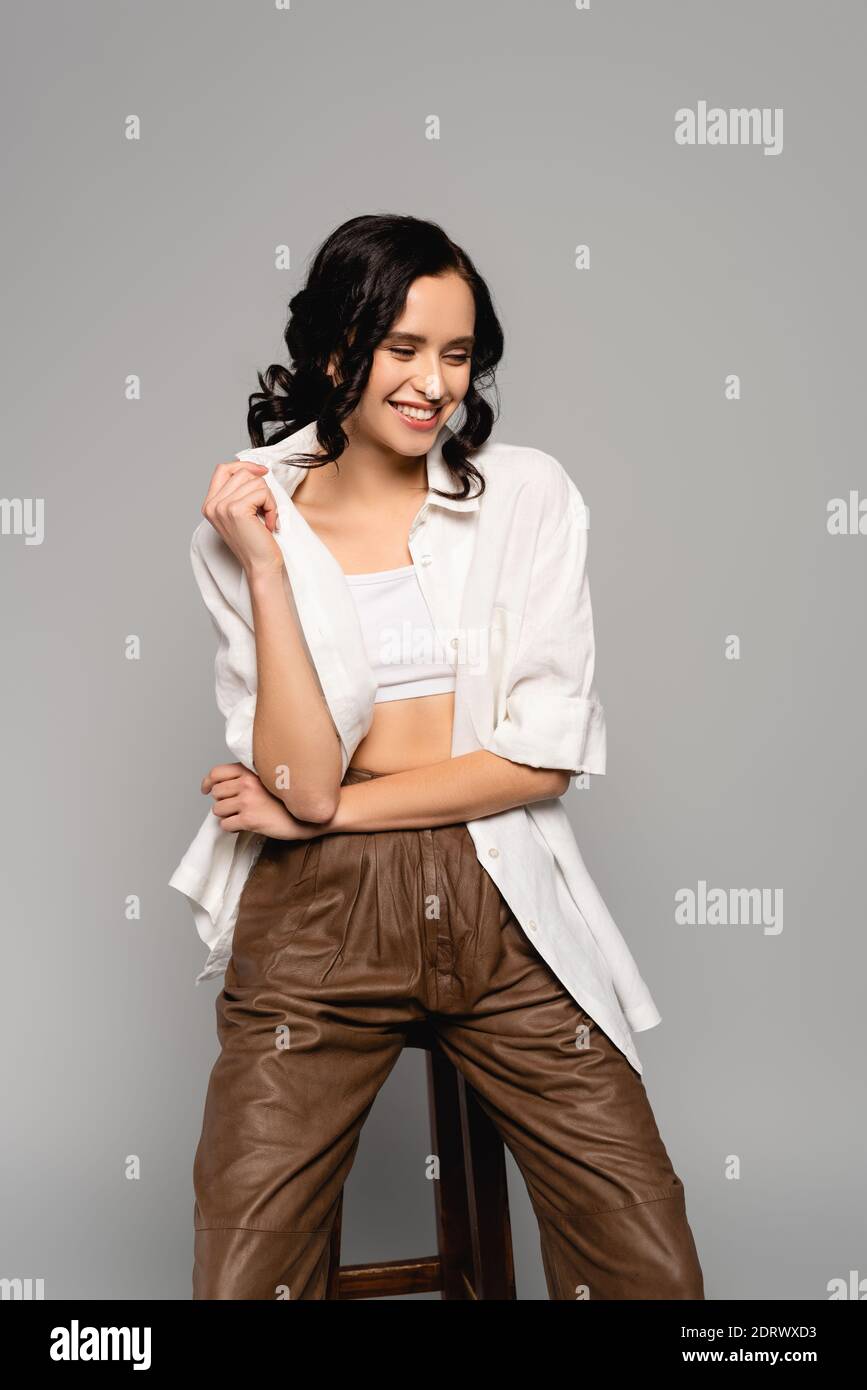 Cheerful brunette woman in casual clothes looking down while leaning on ...