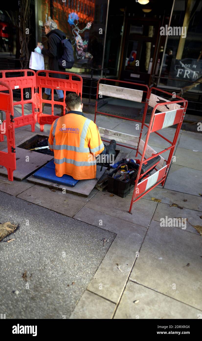 London, England, UK. BT Openreach workman in a hole in the pavement ...