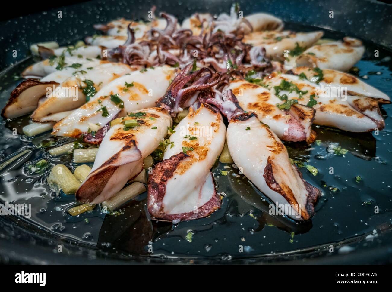 Squid paella closeup view with young garlics Stock Photo - Alamy