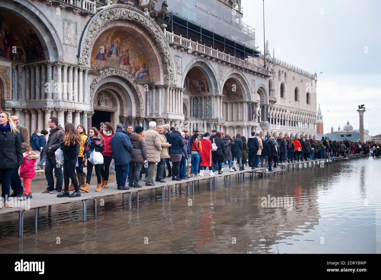 Tourists standing in line in St. Mark's Square flooded by high tide ...