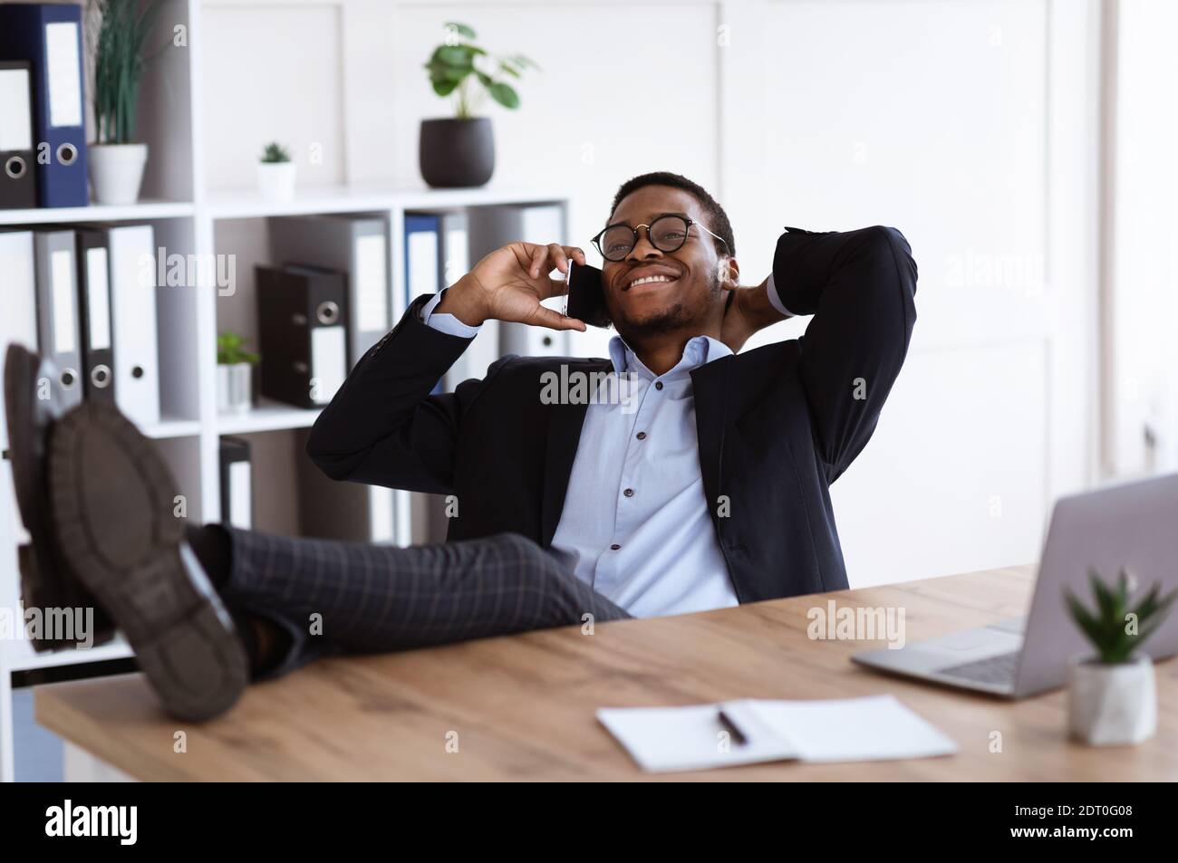 Relaxed black manager sitting with legs on desk, having conversation ...