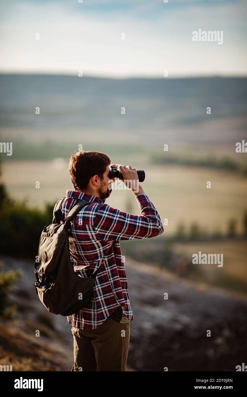 Guy looking at binoculars in hill. man in t-shirt with backpack. Young ...