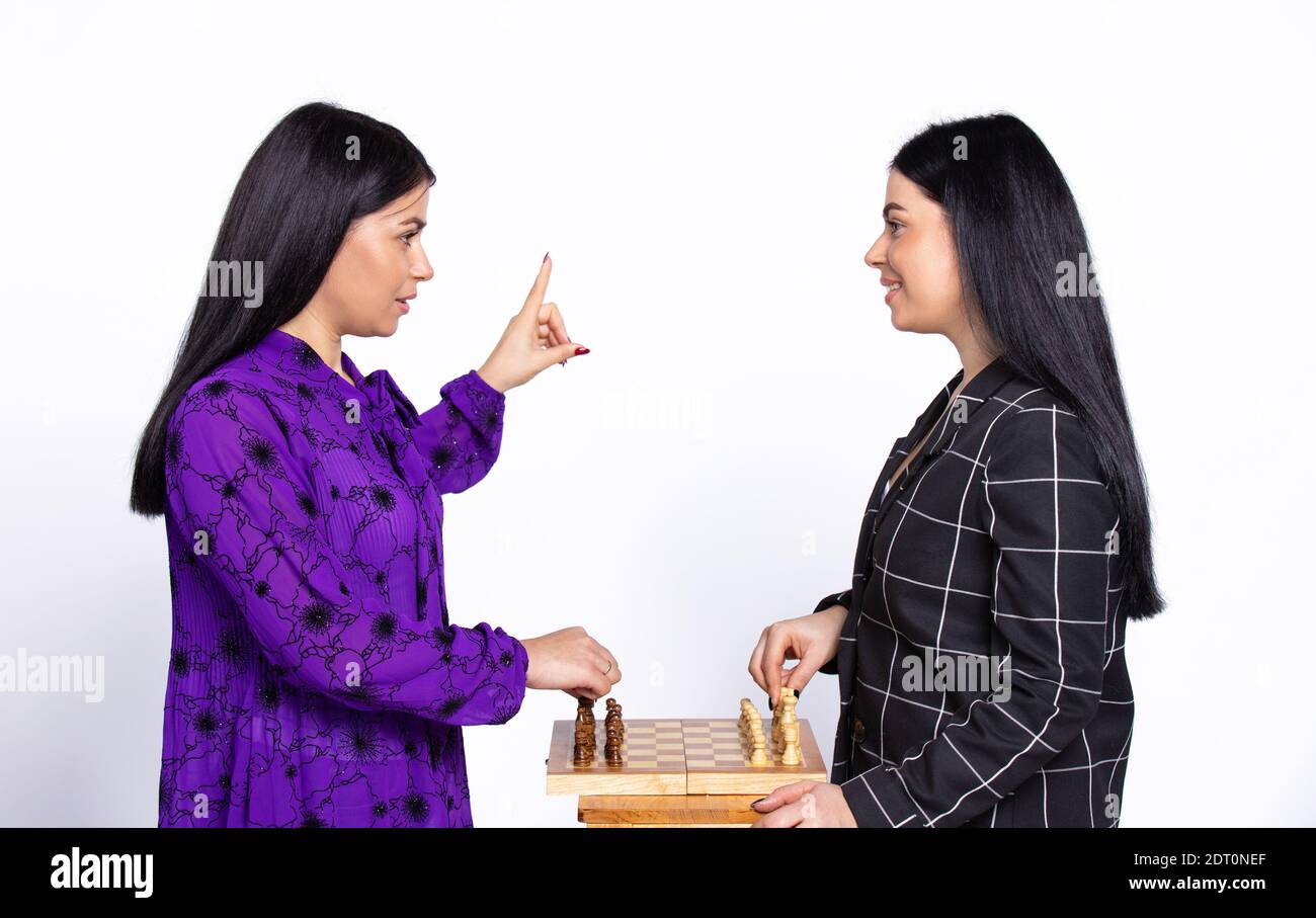 Twins play chess on a white background. One of the girls points to the ...