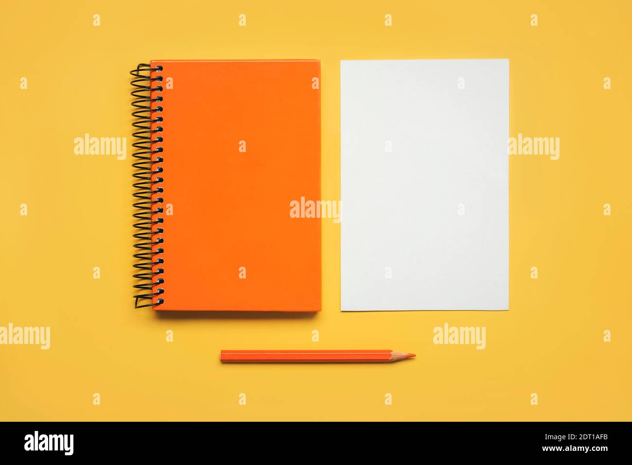 orange spiral notepad with a sheet of white paper and orange pencil on ...