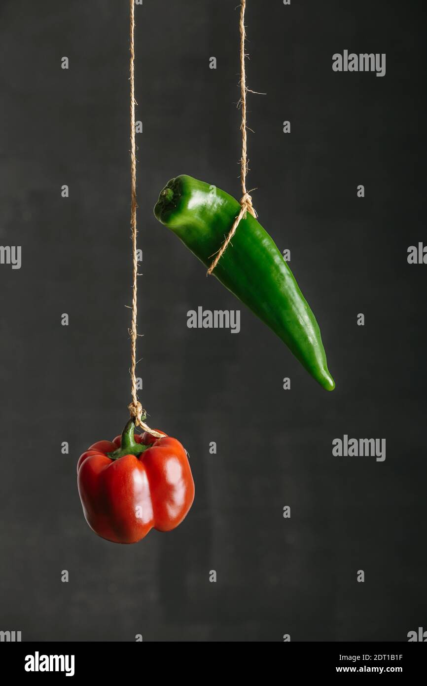 Red and green peppers suspended on a string against black background ...