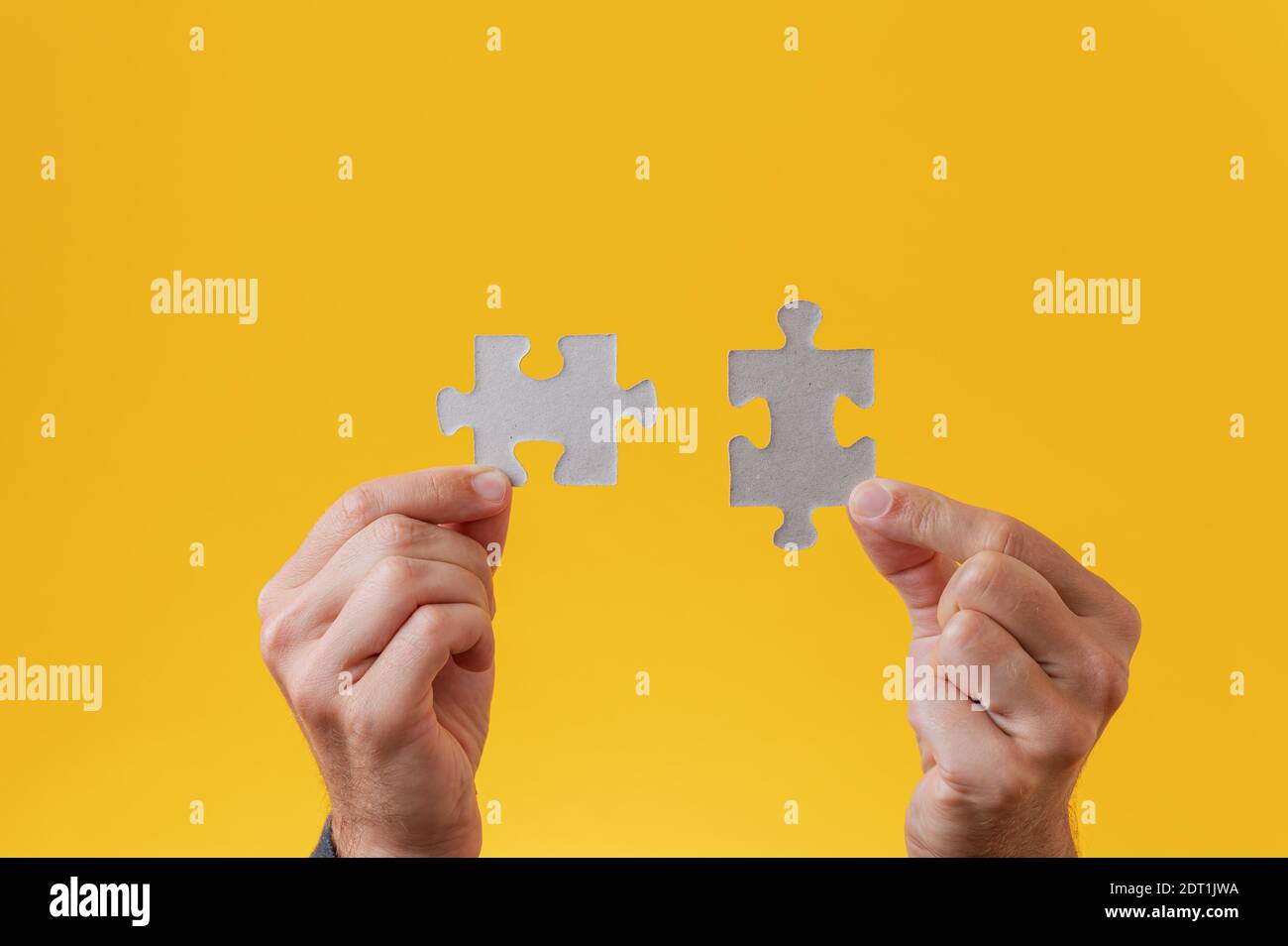 Male hands holding two blank matching puzzle pieces over yellow ...