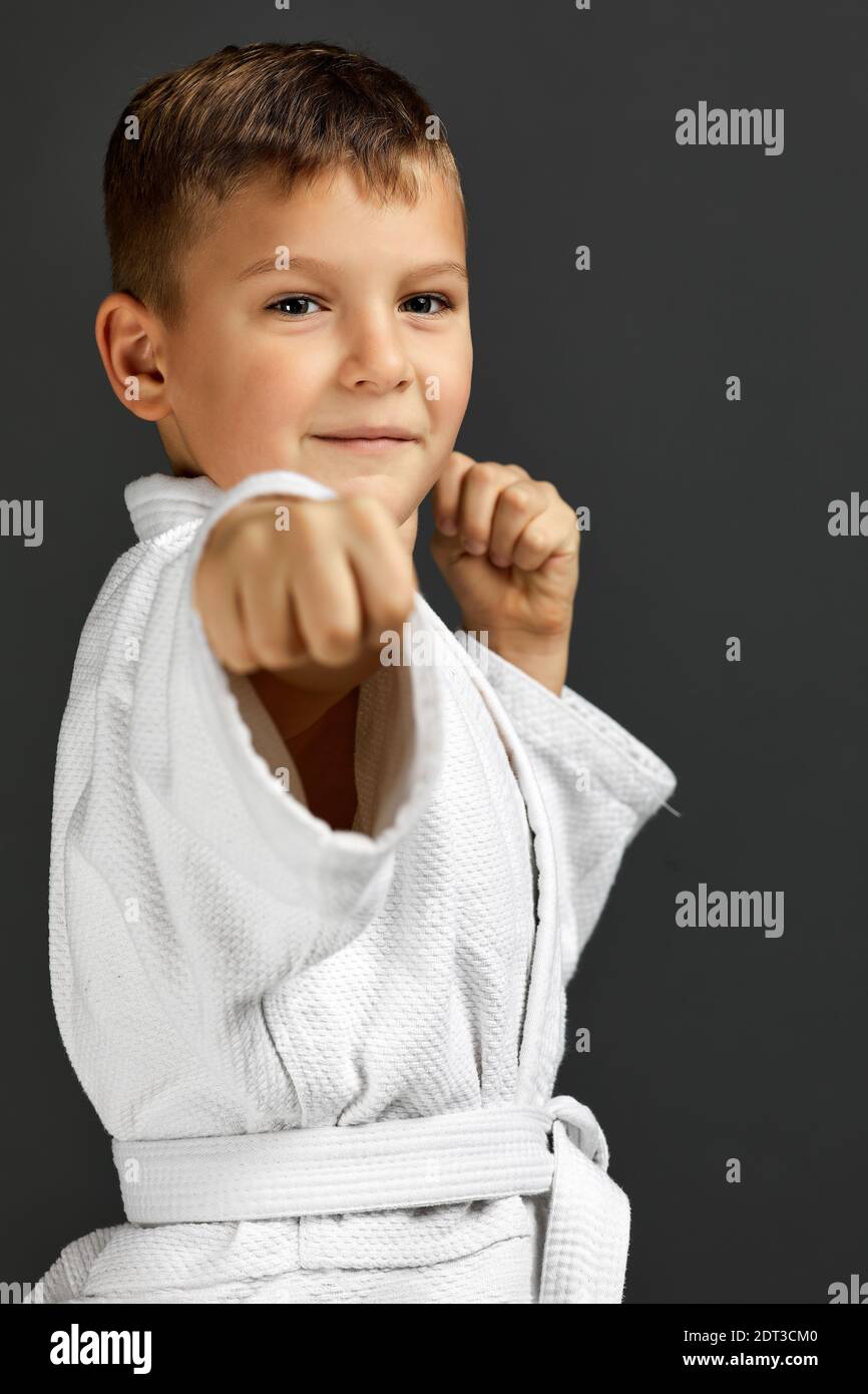 portrait of little child boy in a white karate kimono over gray ...