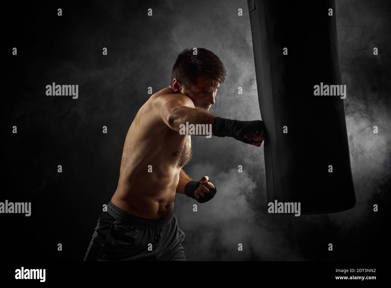 sporty shirtless boxer in black boxing wraps punching in boxing bag on ...