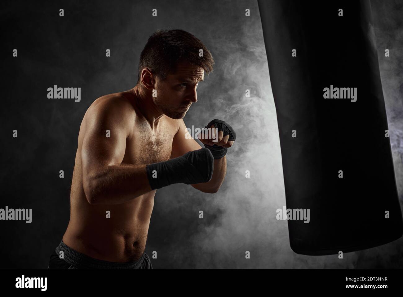Male boxer training defense and attacks in boxing bag on black ...