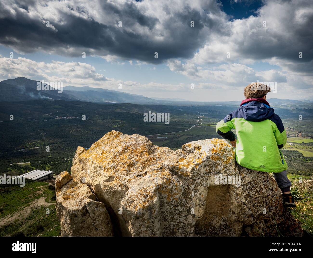Rear view of boy sitting on rock at mountain Stock Photo - Alamy