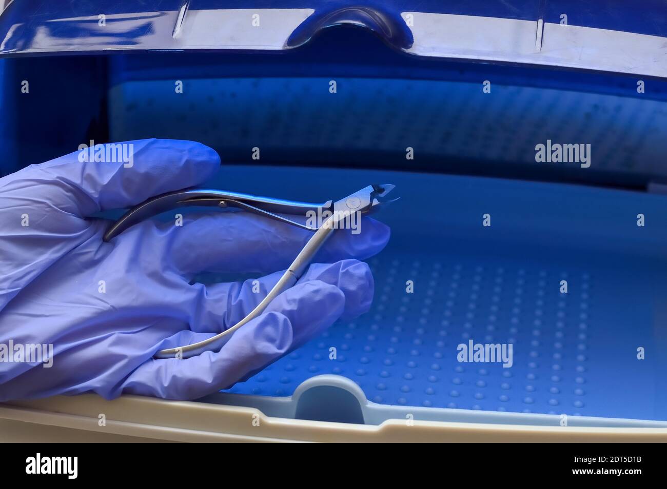 hand in a blue medical glove with manicure and pedicure forceps after ...