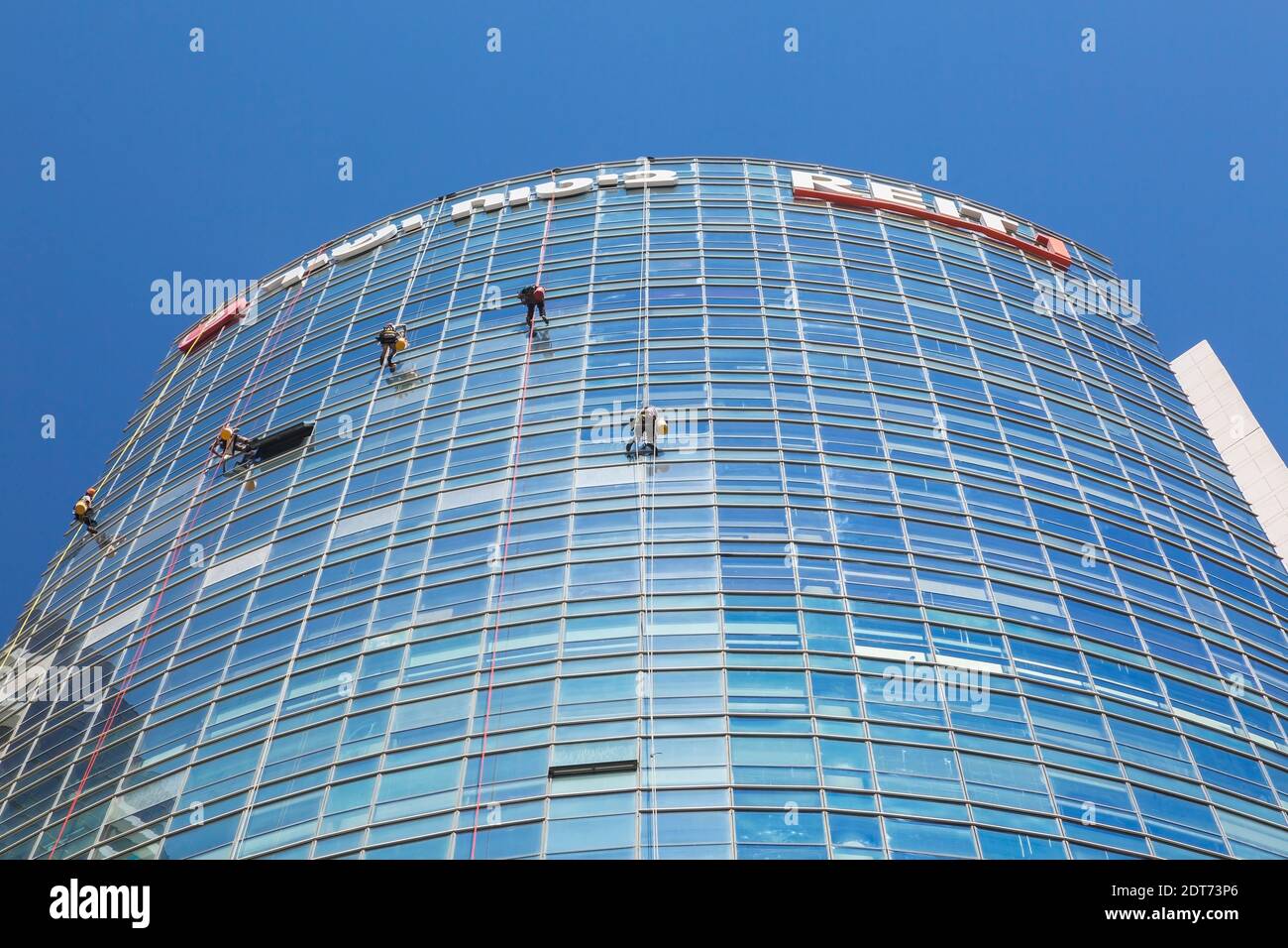 Window washers hanging from ropes on outside of modern curved ...