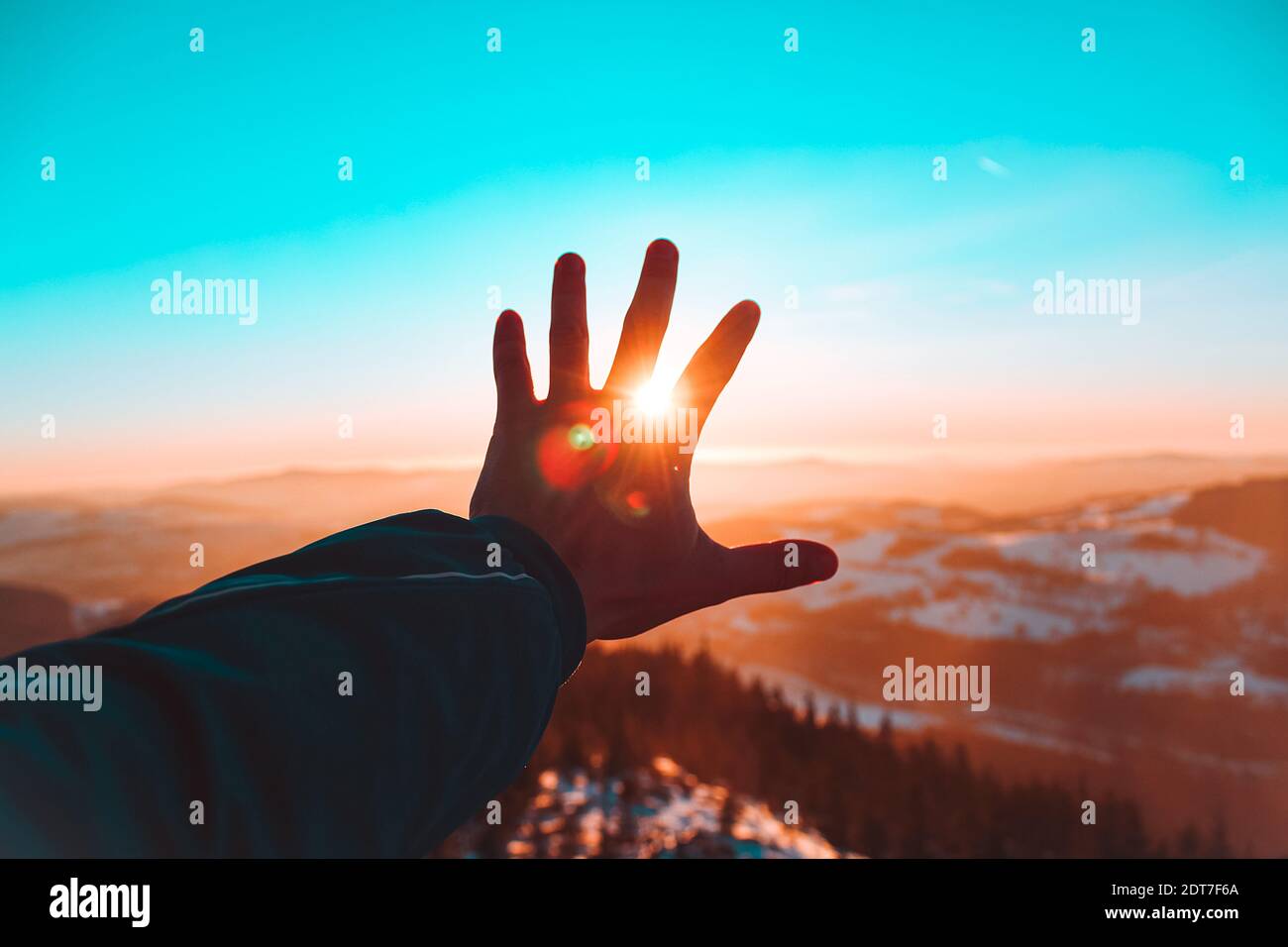 Male left hand covering the sun in Czechia mountines covered with snow ...