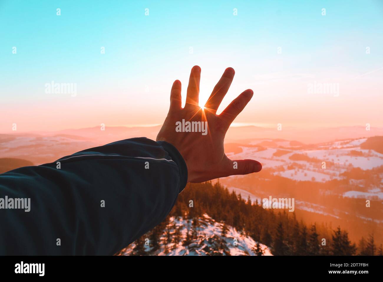 Male left hand covering the sun in Czechia mountines covered with snow ...