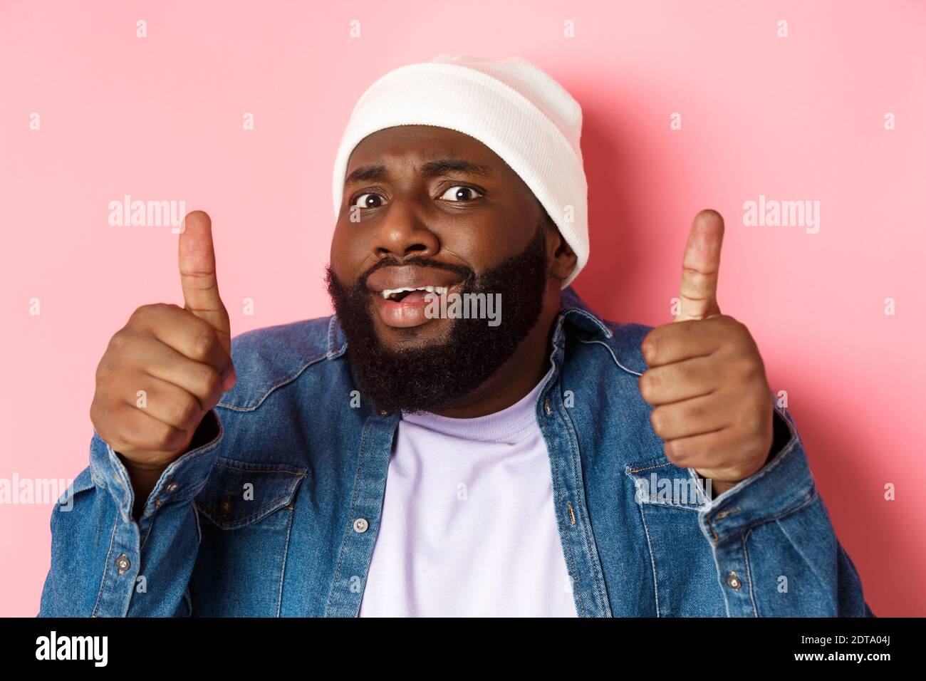 Close-up of awkward Black man in beanie showing thumbs-up but feeling ...