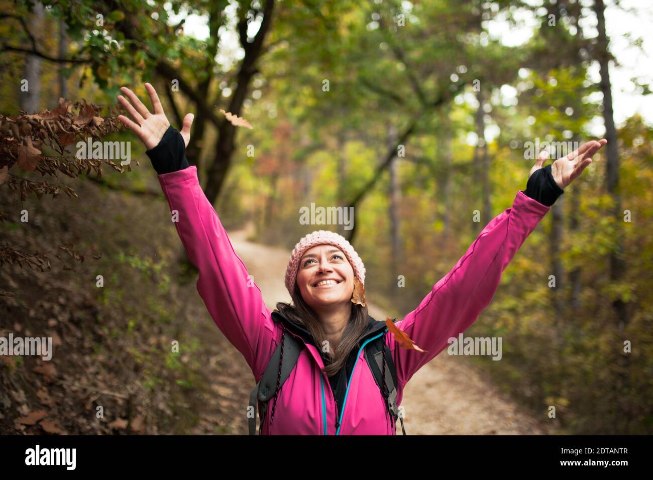 Hiking girl in pink on a trail in the forest. Hands up enjoying the ...