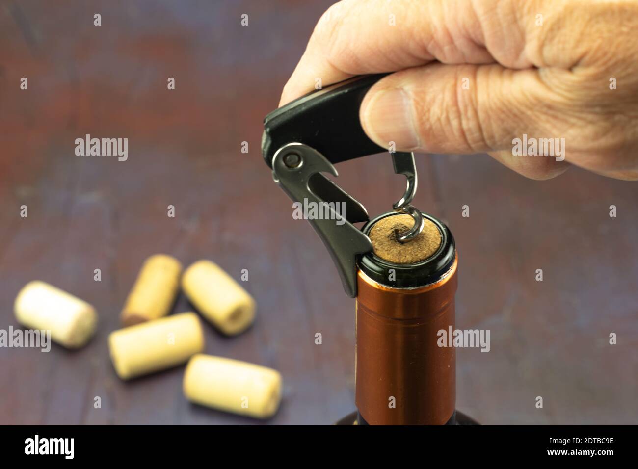 A hand pulling a corkscrew out of its green glass bottle and copper ...