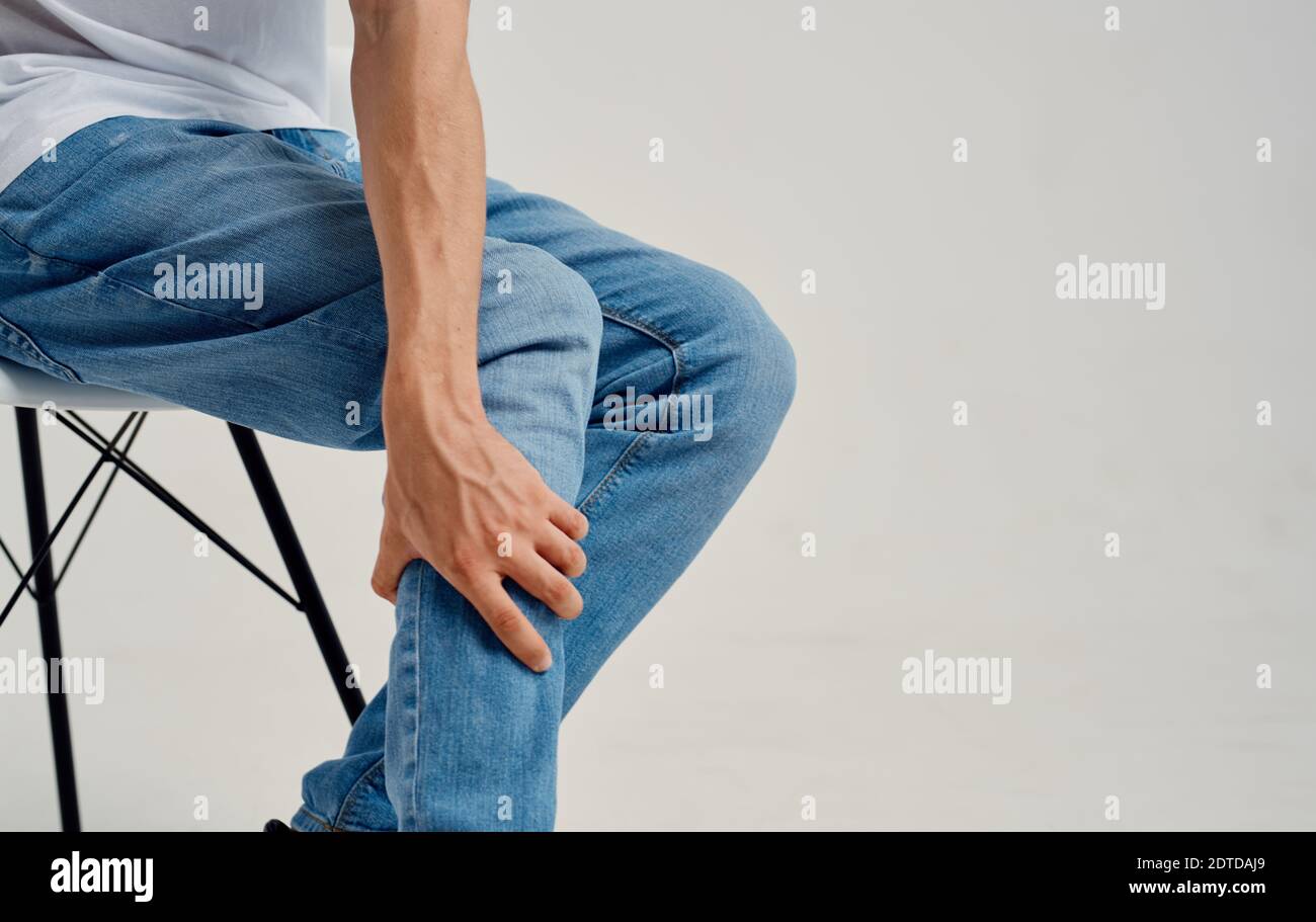 man in jeans sitting on a chair and touching his leg with his hands ...