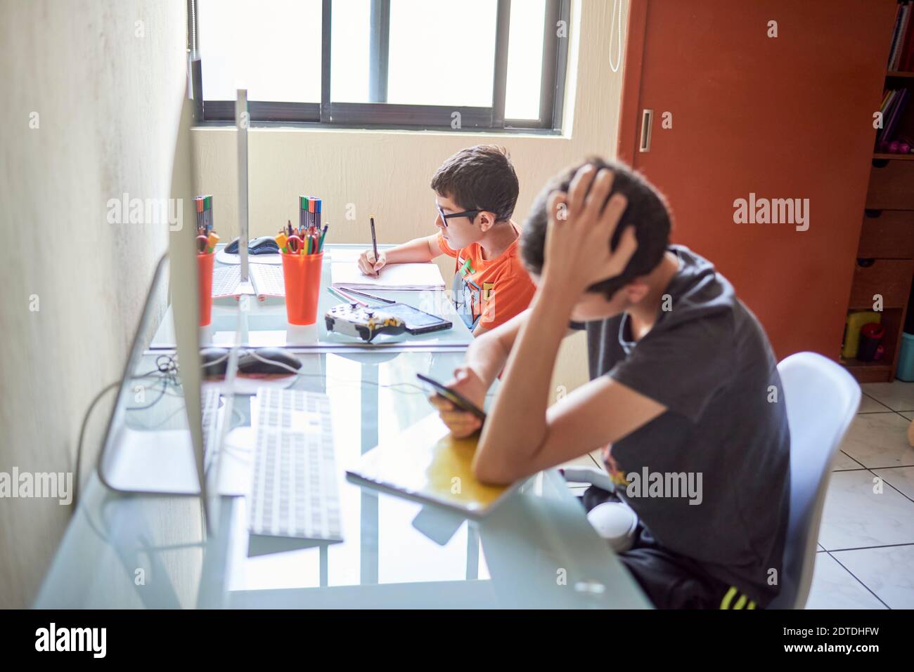 Two boys (8-9, 14-15) learning at desk at home during Covid-19 lockdown ...