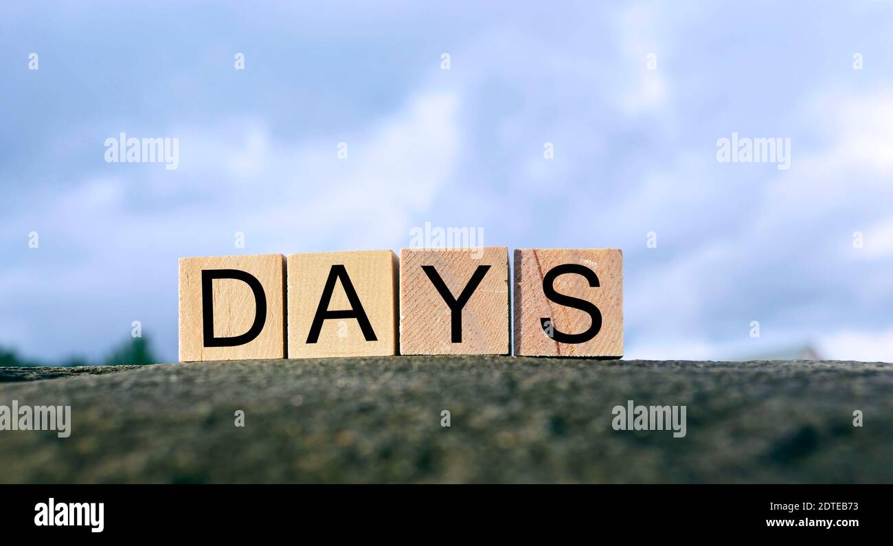 Days text on wooden cube block on top of big stone with blurred sky ...