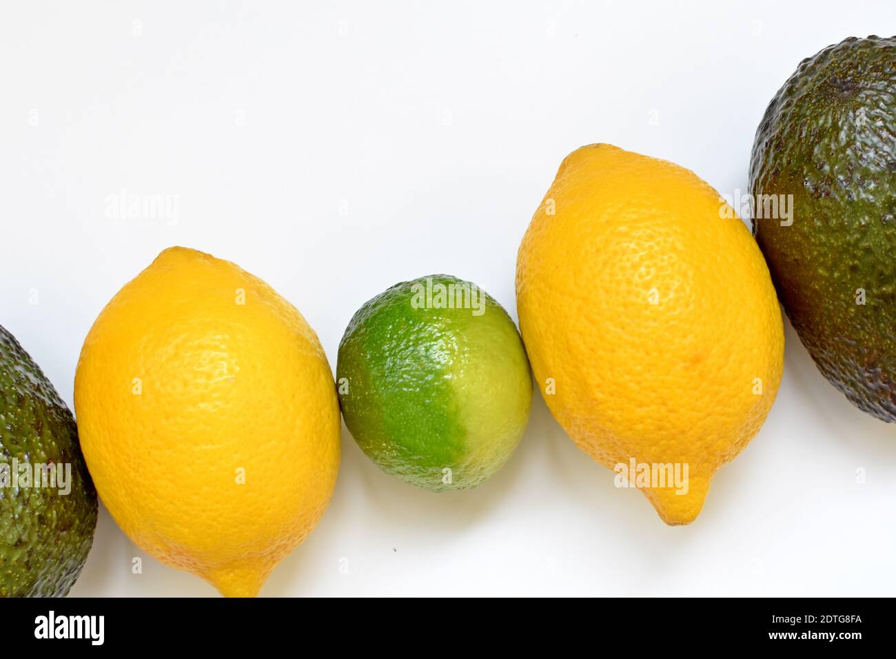 Top table with lemons, lime and avocado in a diagonal row on white ...