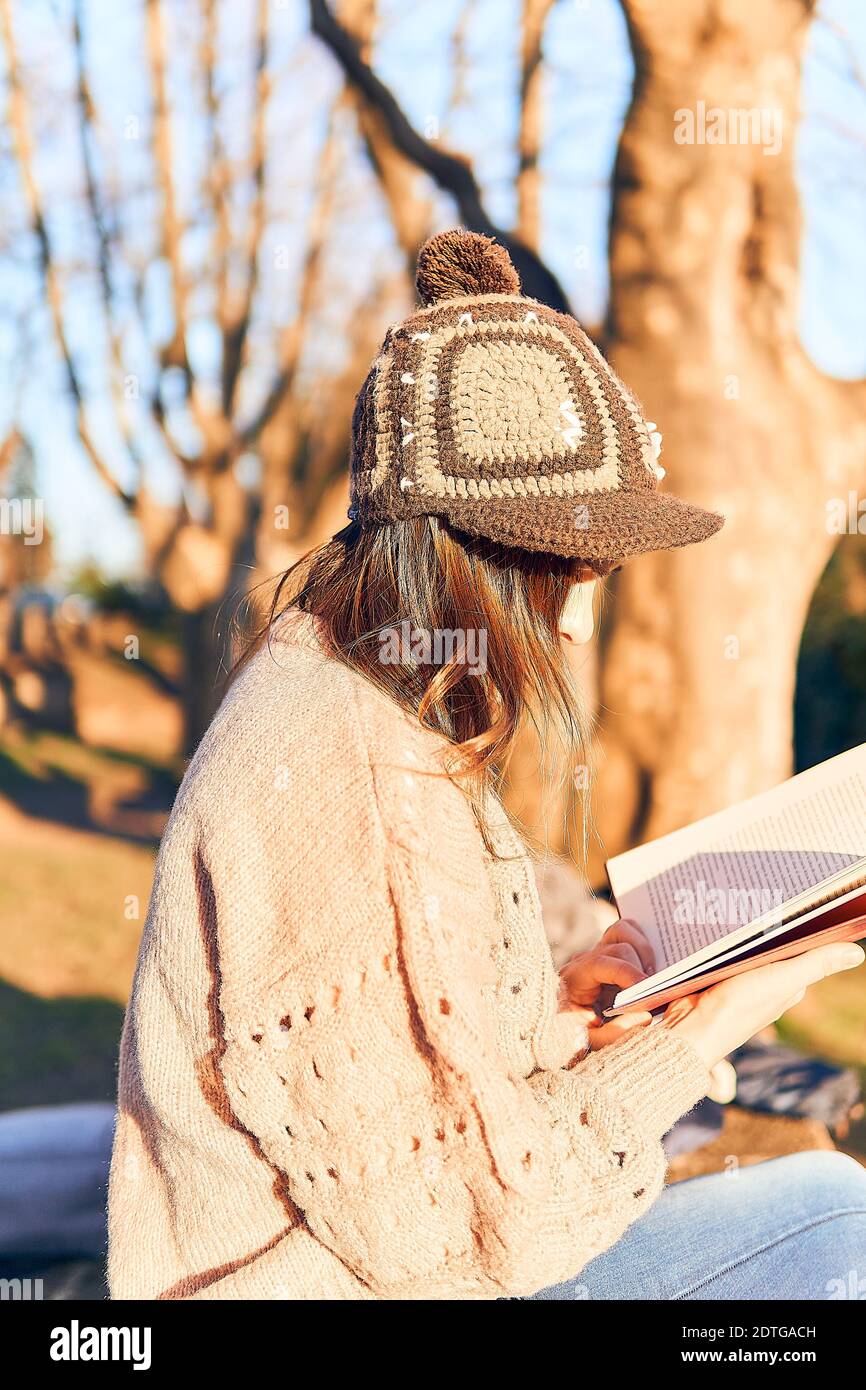 beautiful woman with cap reading a book in a park at winter or spring ...