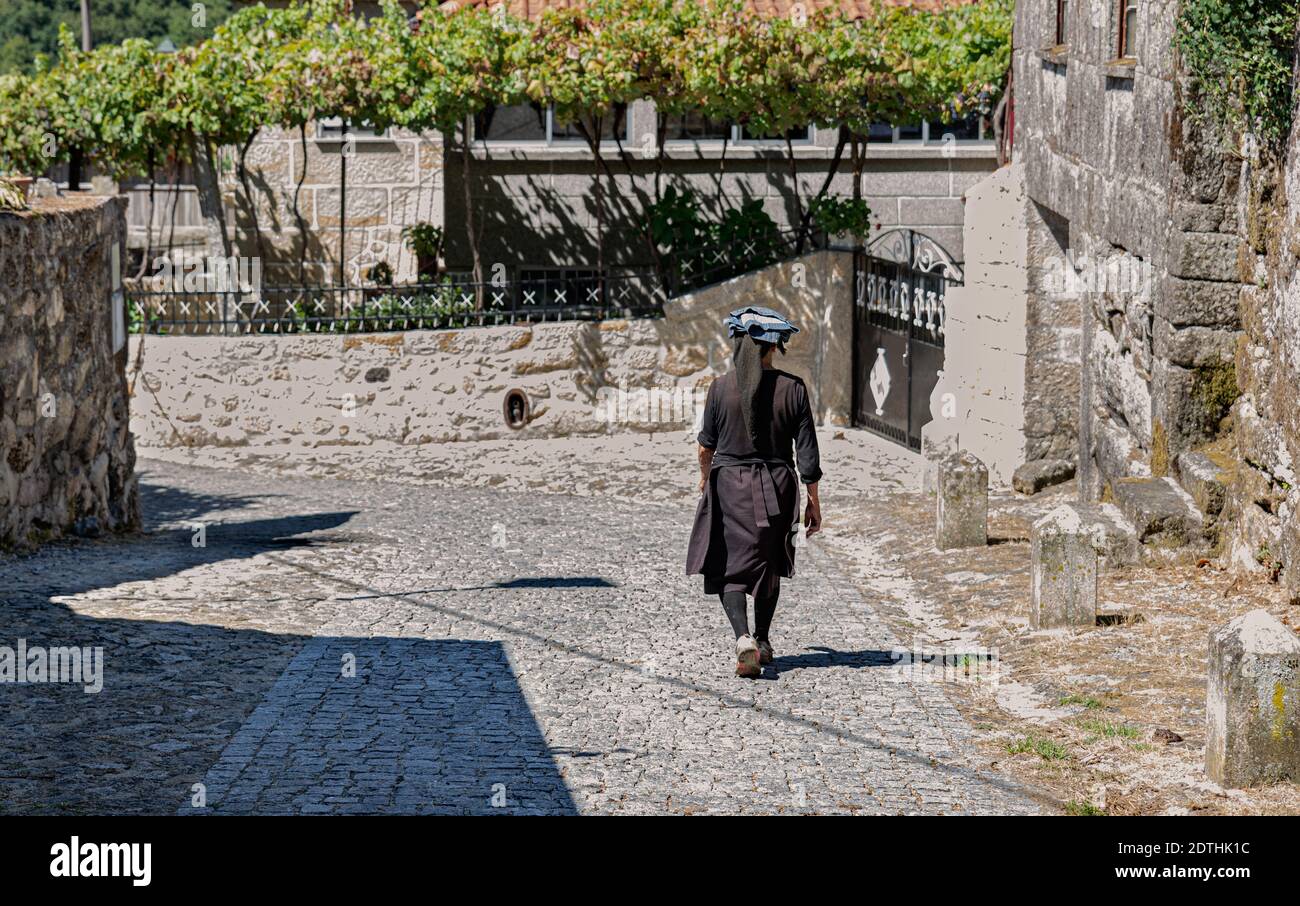 Peasant woman dressed in black walking on a cobbled street in a village ...