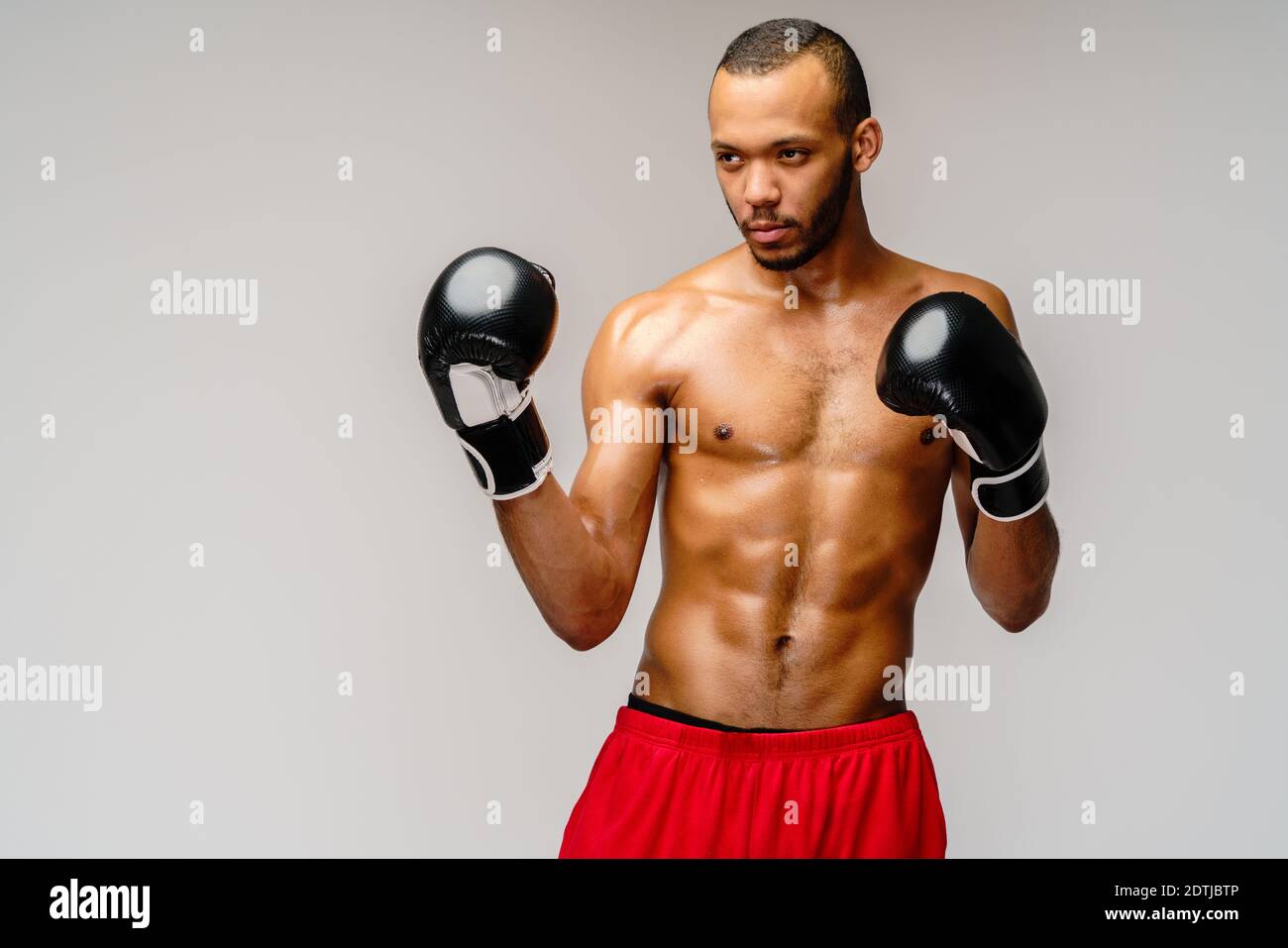 Confident young African boxer in boxing gloves standing over light grey ...