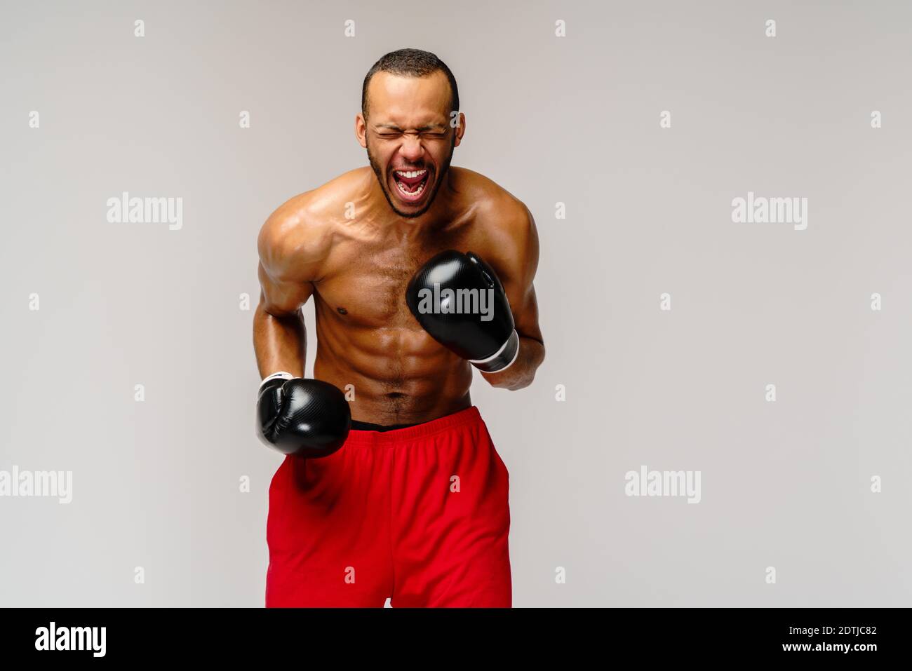 Confident young African boxer in boxing gloves standing over light grey ...