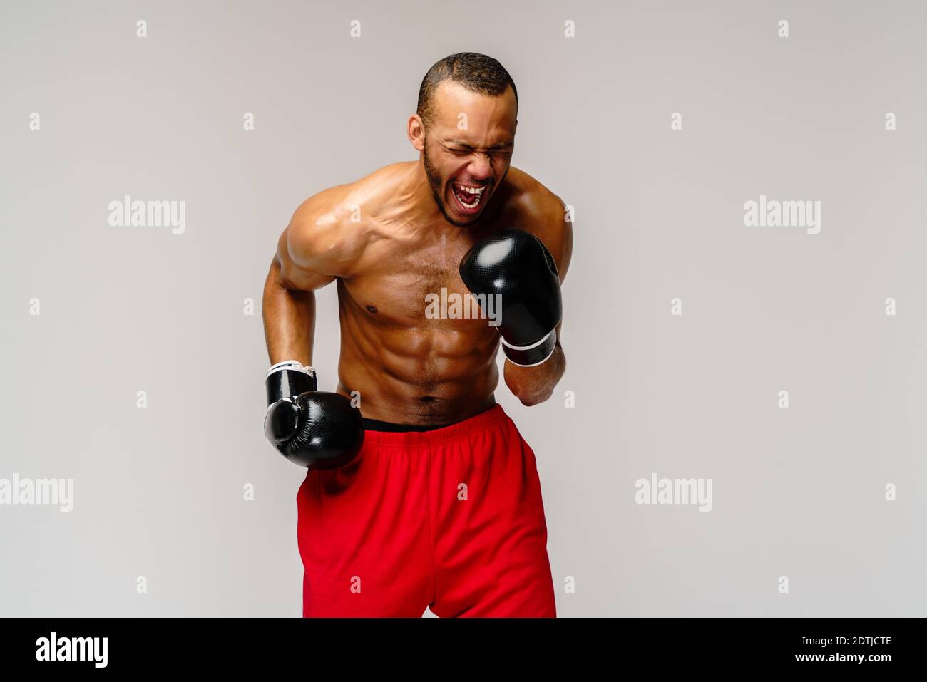 Confident young African boxer in boxing gloves standing over light grey ...