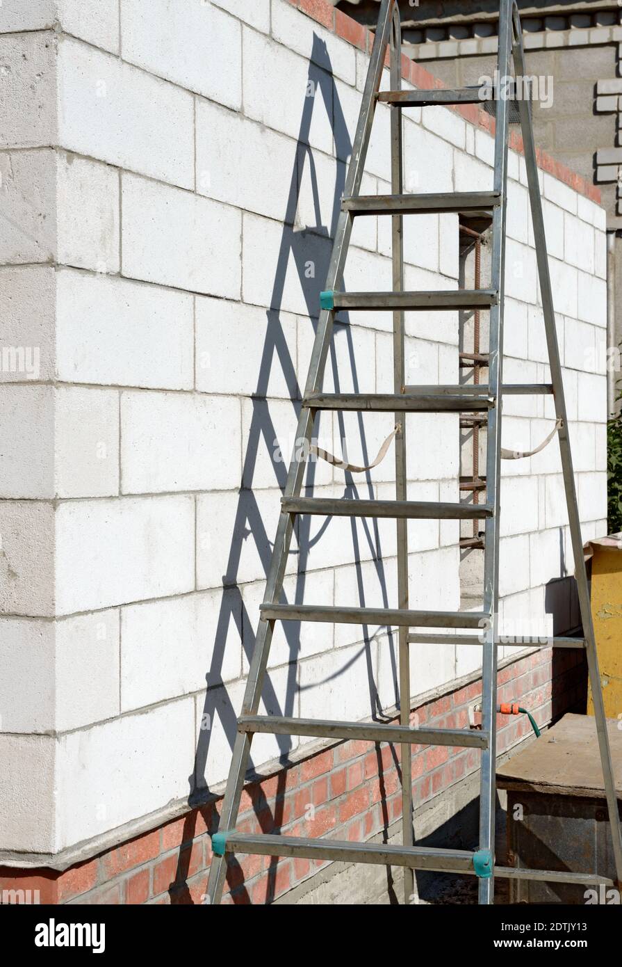 Close-up old used metal dismountable scaling ladder on light wall of ...