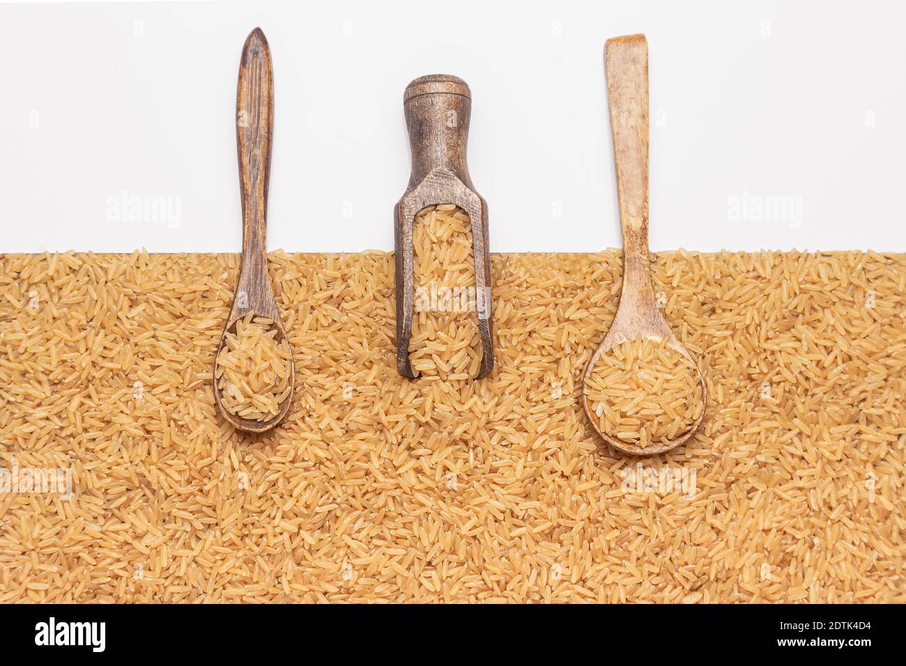 Three wooden spoons with brown rice on white and brown rice background ...
