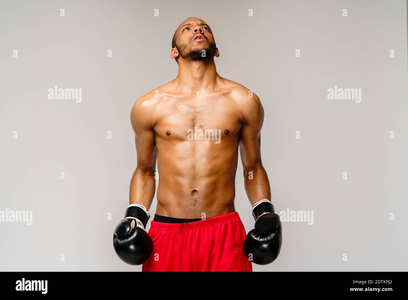Confident young African boxer in boxing gloves standing over light grey ...