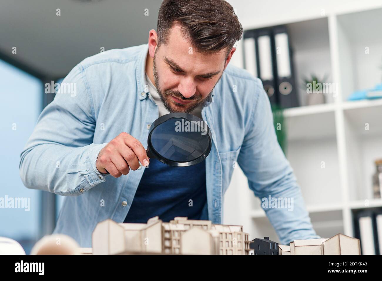 Architect inspector examines a house model using a magnifying glass ...