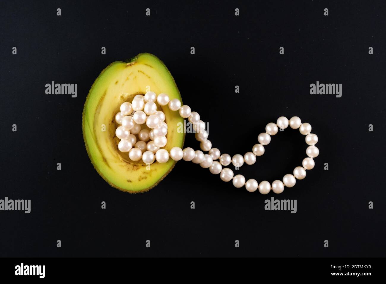half an avocado with pearls on a black background. surrealism ...