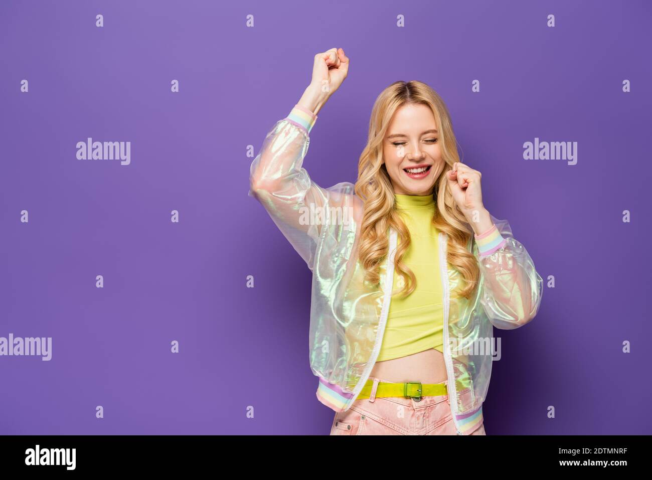 happy blonde young woman in colorful outfit showing yeah gesture on ...